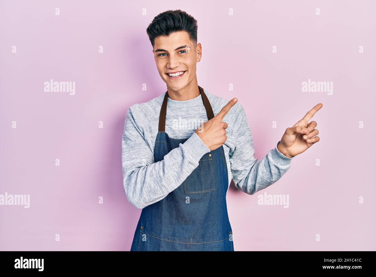 Young hispanic man wearing apron smiling and looking at the camera ...