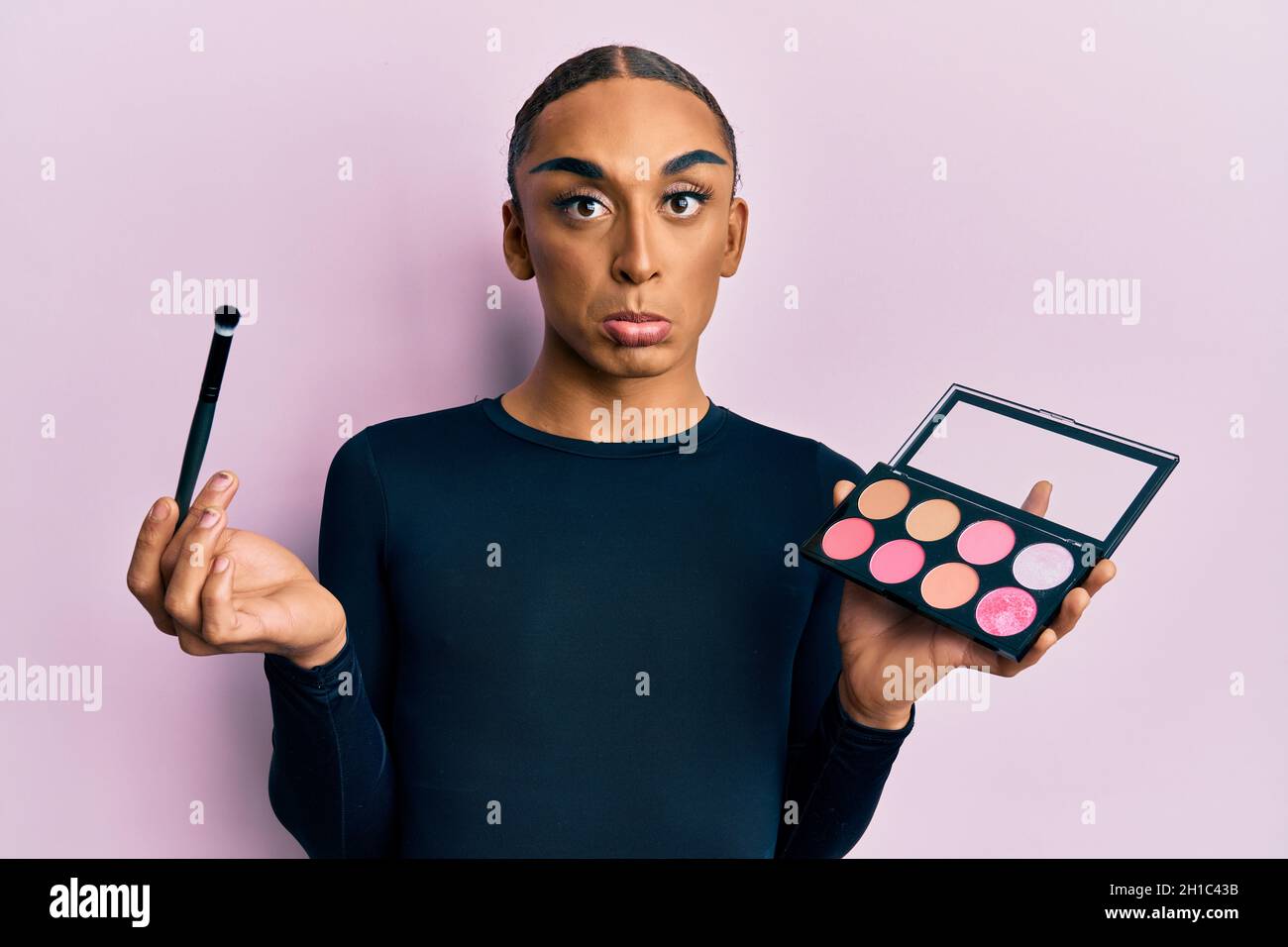 Hispanic man wearing make up and long hair holding makeup brush and ...