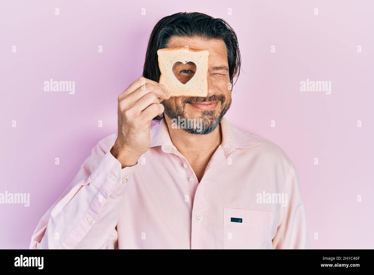 Middle age caucasian man holding bread loaf with heart shape looking ...