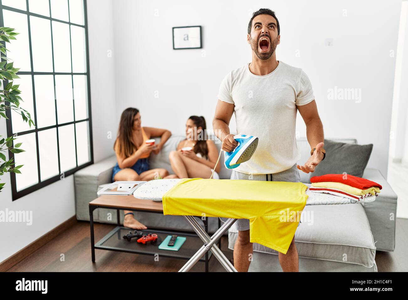 Young hispanic man ironing clothes at home angry and mad screaming ...
