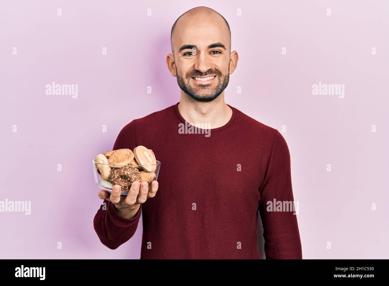 Young bald man holding sweet pastries looking positive and happy ...