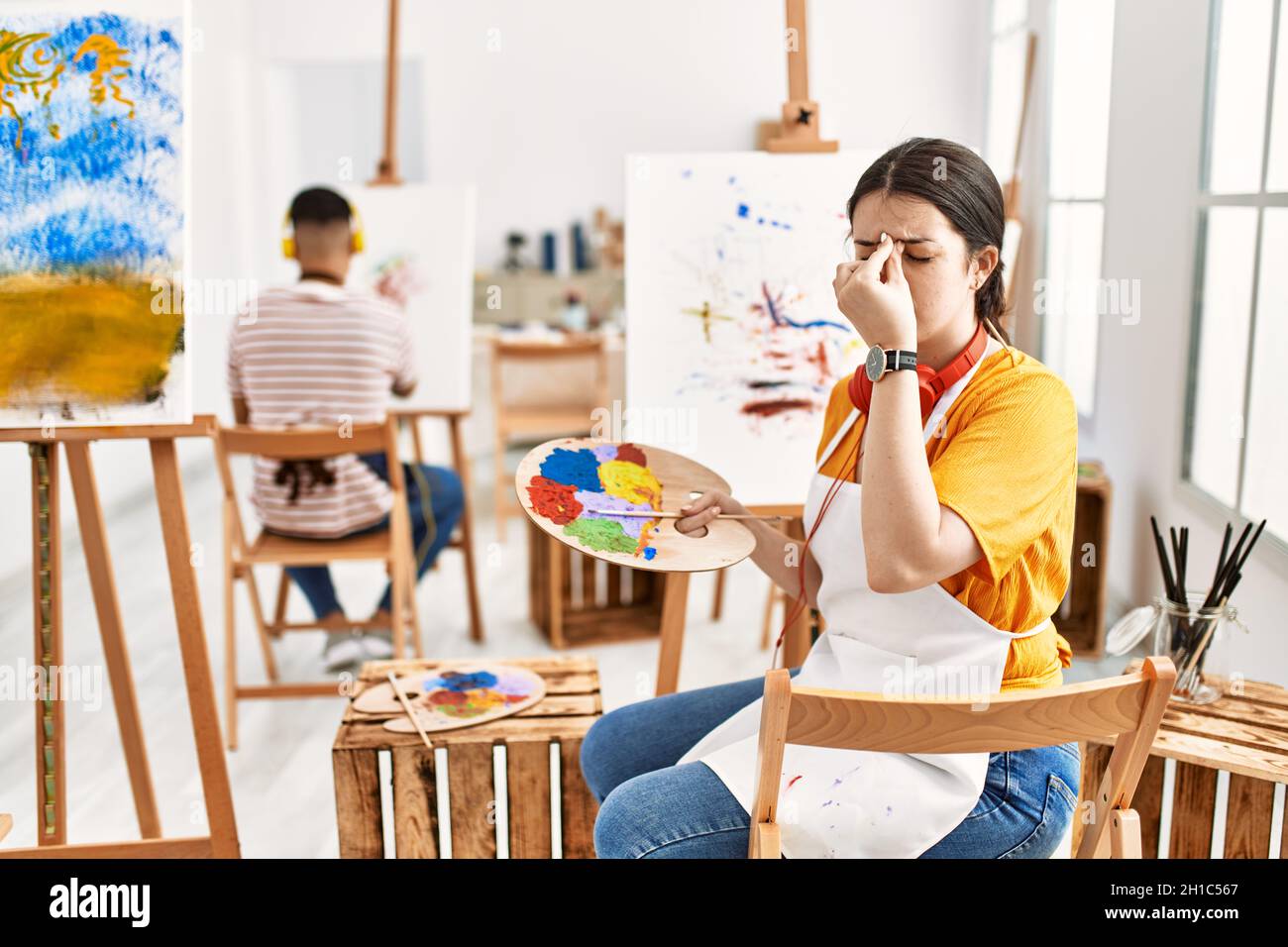 Young artist woman painting on canvas at art studio tired rubbing nose ...