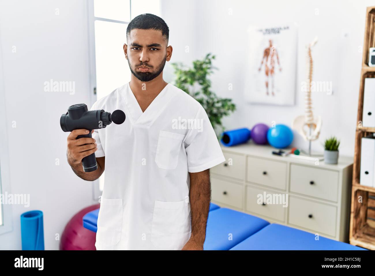 Young indian physiotherapist holding therapy massage gun at wellness ...