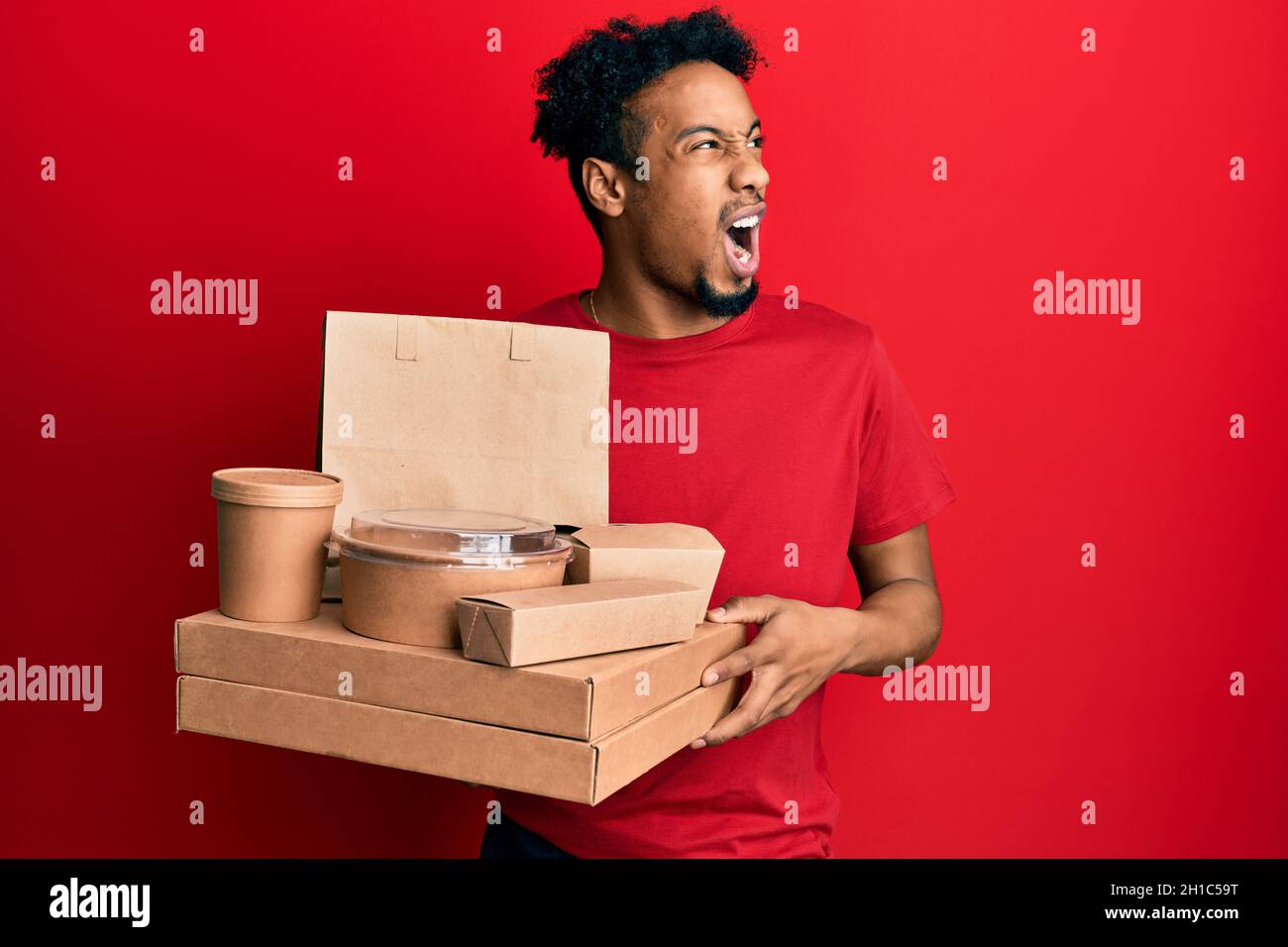 Young african american man with beard holding take away food angry and ...
