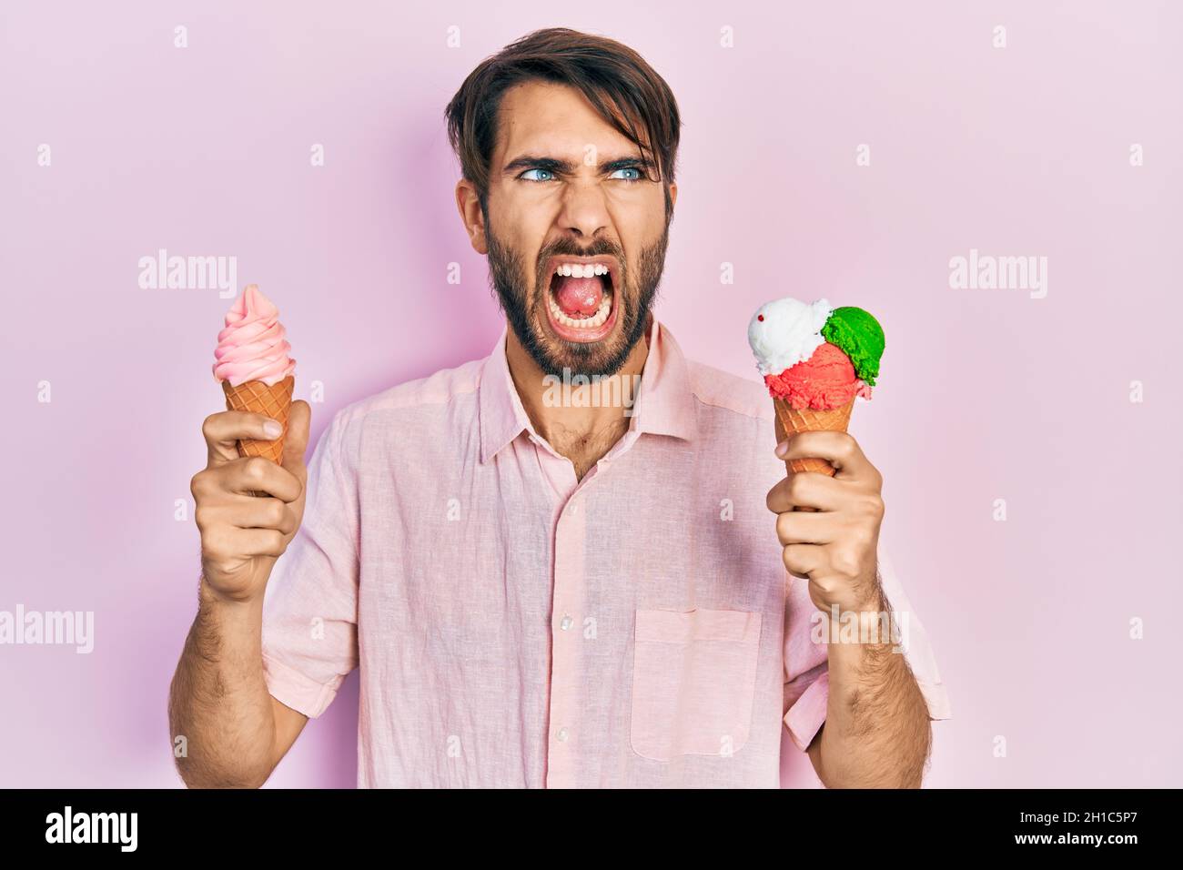 Young hispanic man holding ice cream angry and mad screaming frustrated ...