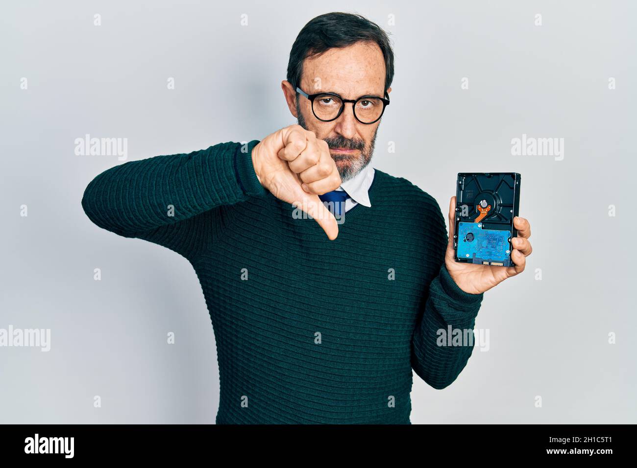 Middle age hispanic man holding hdd disk with angry face, negative sign ...