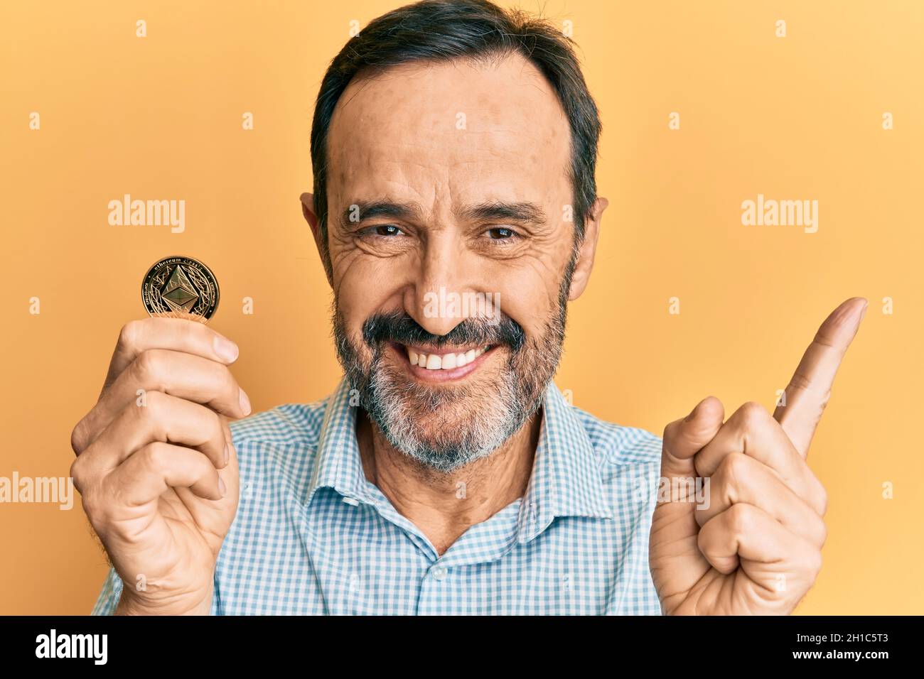 Middle age hispanic man holding virtual currency ethereum coin smiling ...