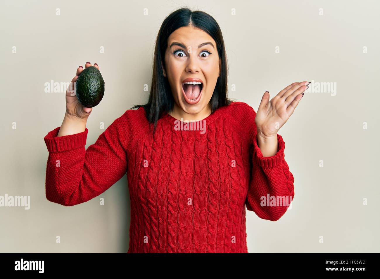 Beautiful brunette woman holding avocado celebrating achievement with ...