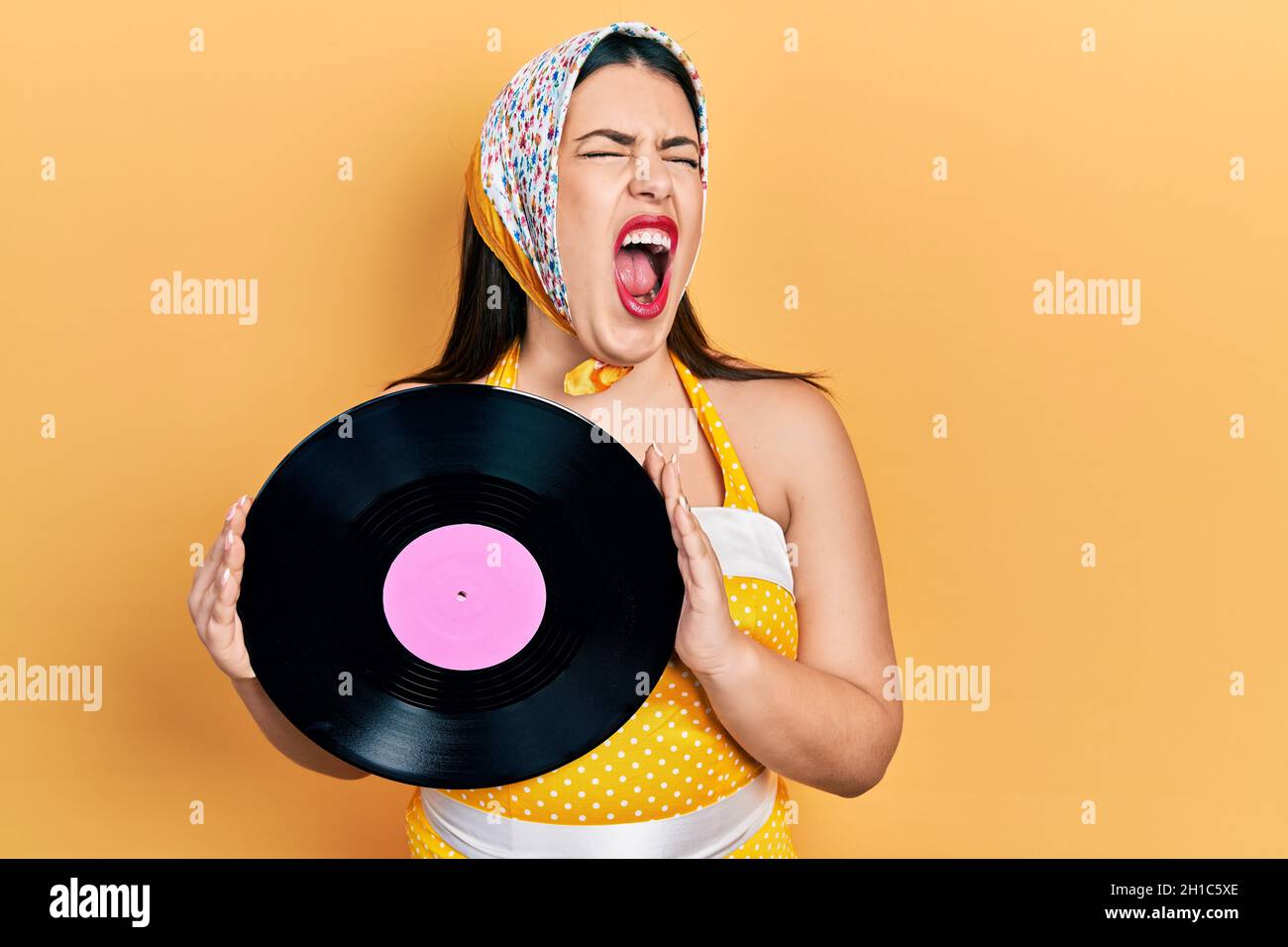 Young hispanic woman wearing pin up style holding vinyl disc angry and ...