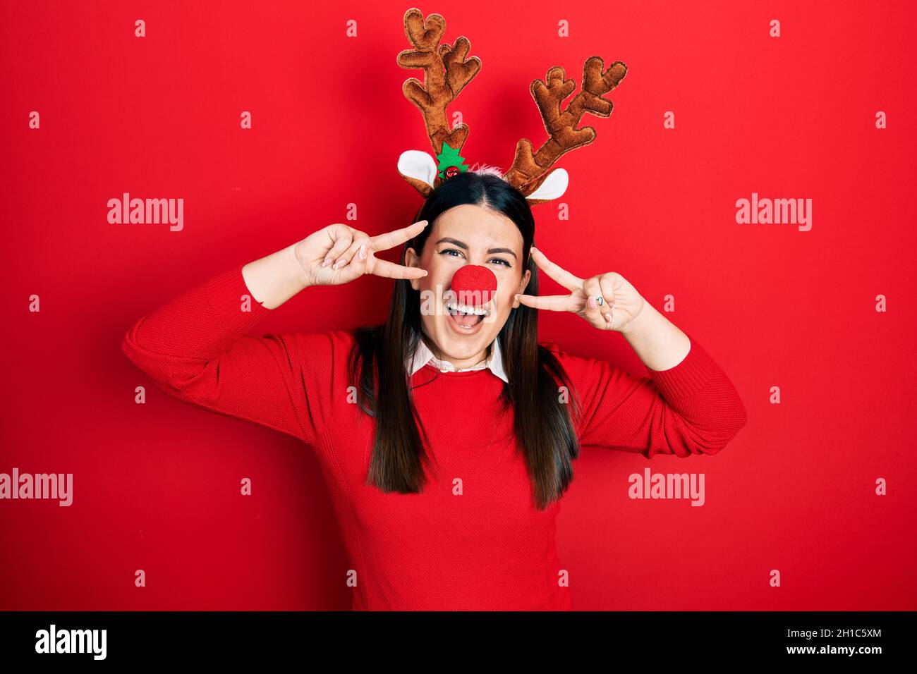 Young hispanic woman wearing deer christmas hat and red nose doing ...