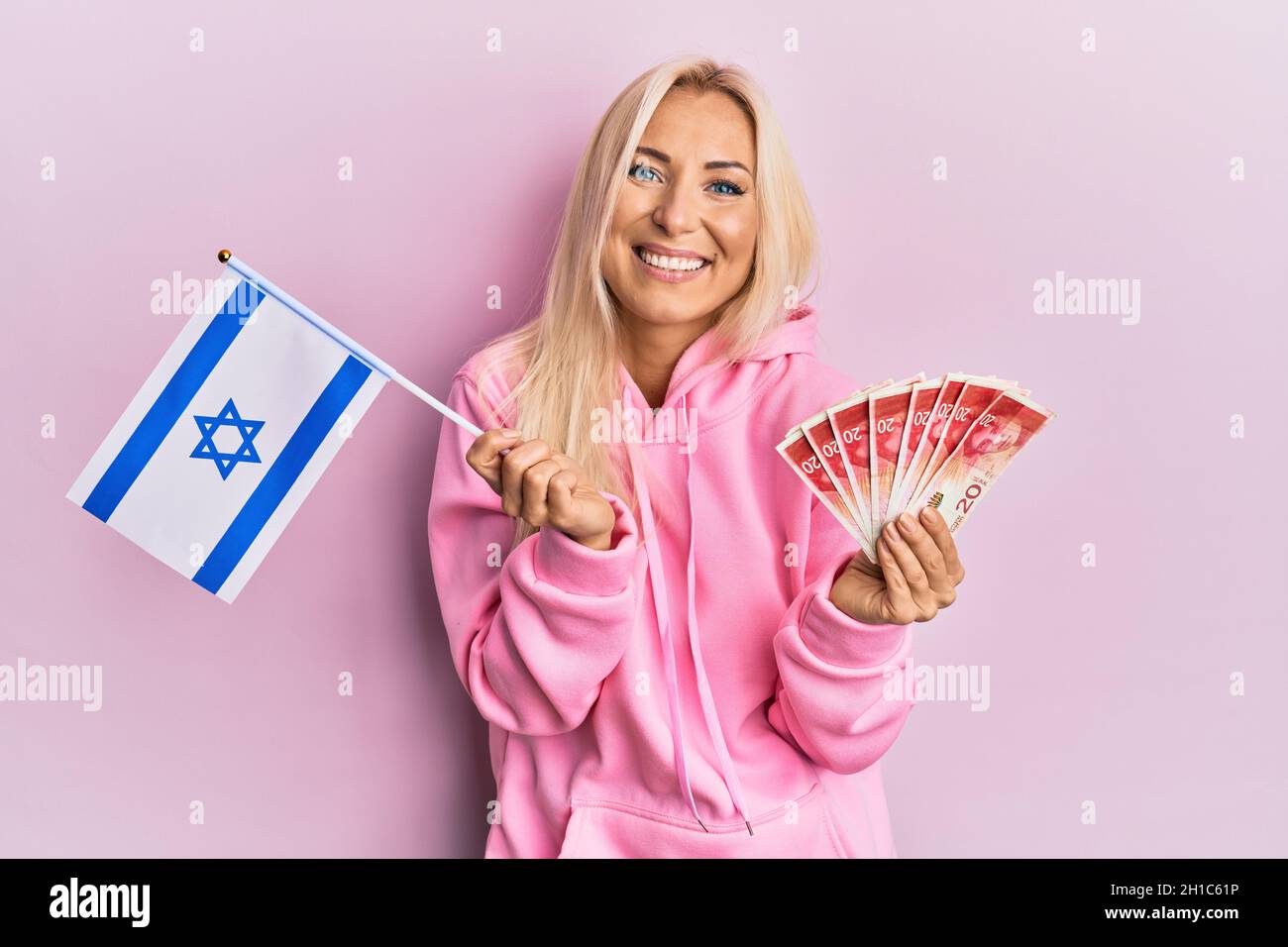 Young blonde woman holding israel flag and shekels banknotes smiling ...