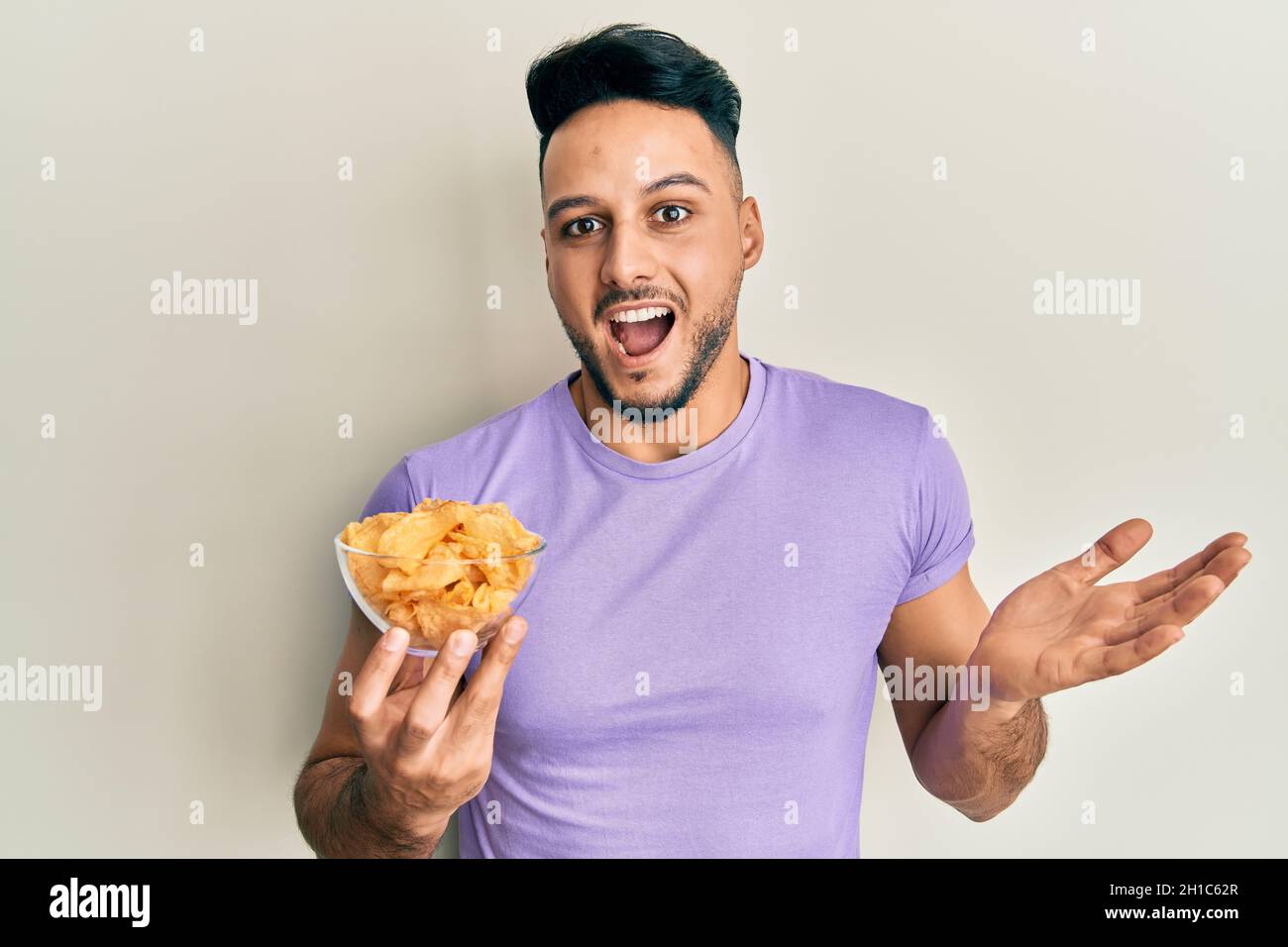 Young arab man holding potato chip celebrating achievement with happy ...