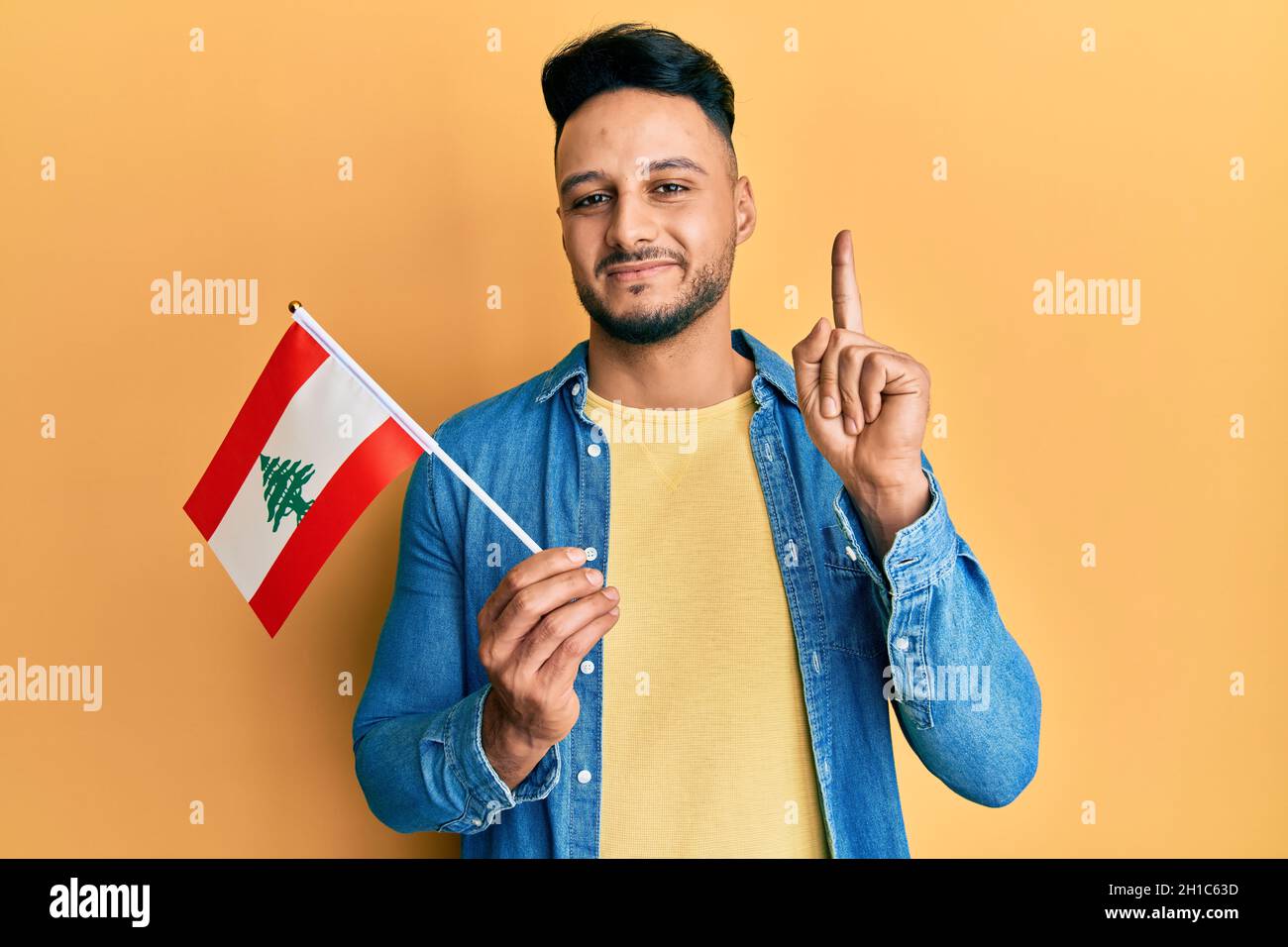 Young arab man holding lebanon flag smiling with an idea or question ...