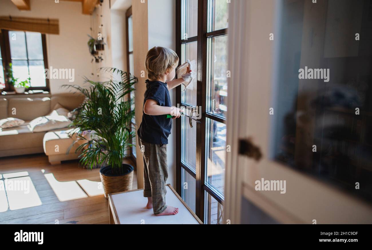 Side view of little boy cleaning windows indoors at home, daily chores ...
