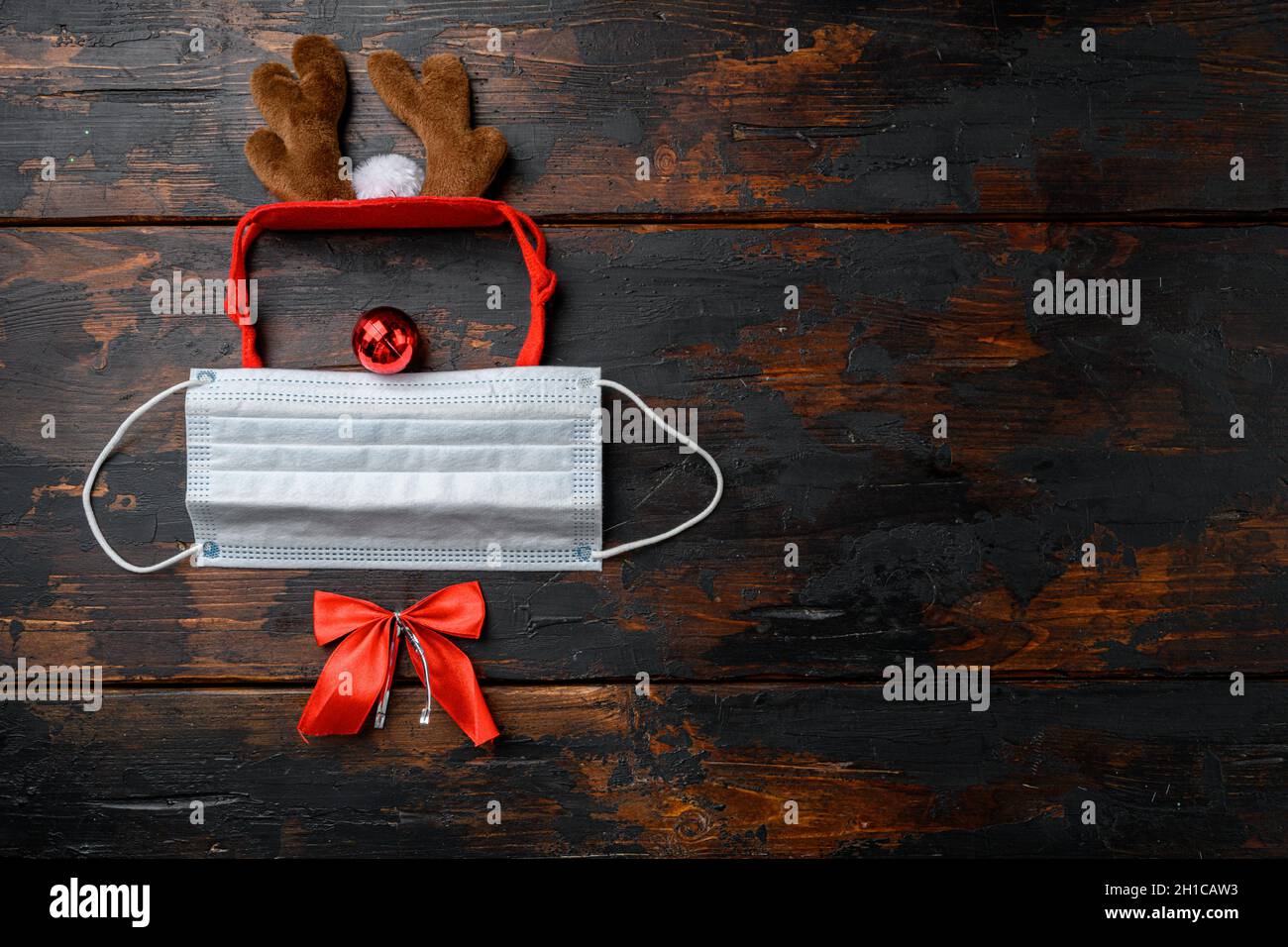 Funny santa from medical mask, red cap set and deer, on old dark wooden ...
