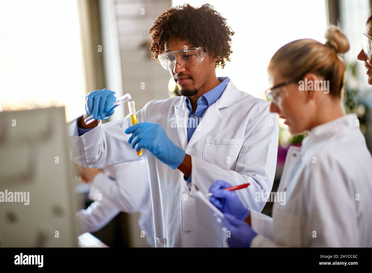 Young students mixing chemicals in a test tube and taking notes about a ...