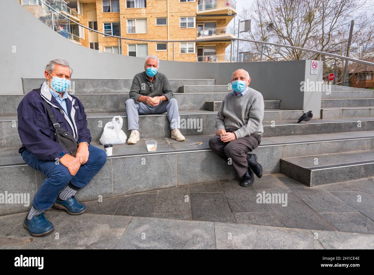 Three older men sitting separated but together on large concrete steps ...