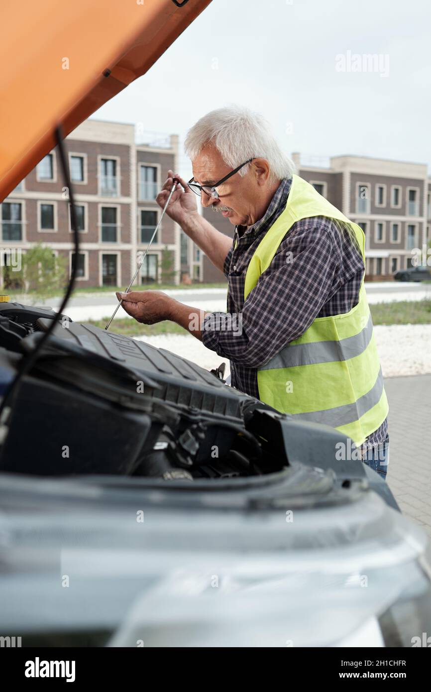 Senior bus driver with handtool checking motor while bending over open ...