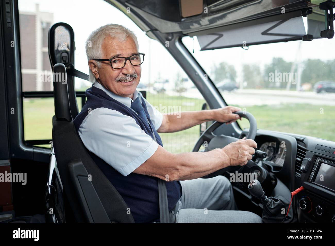 Happy aged driver of intercity bus holding by steering wheel during ...
