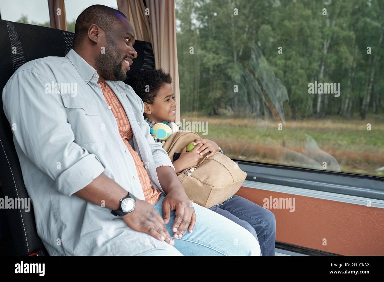 Young father and cute son with backpack looking through bus window ...