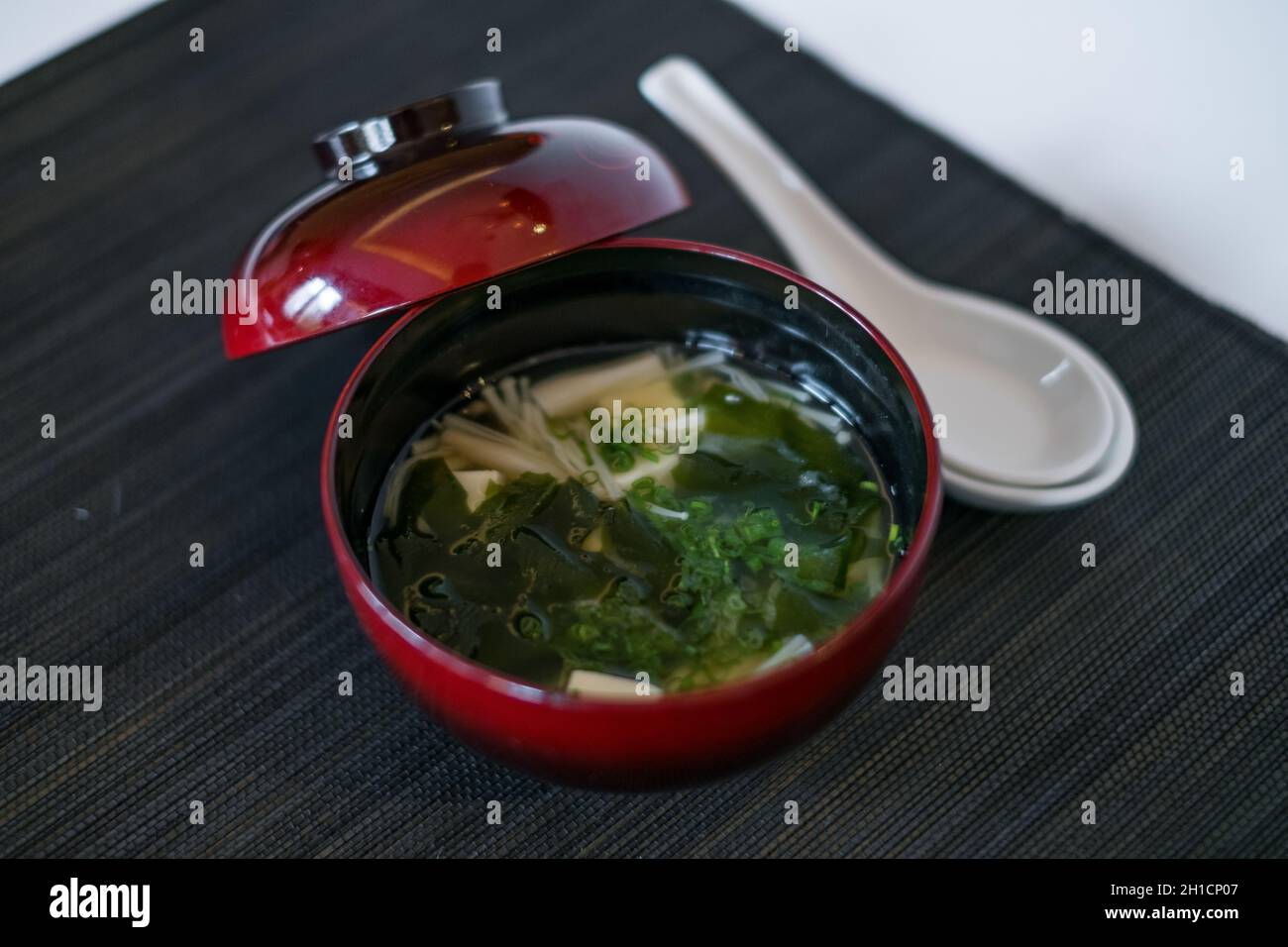 Miso soup in the dark red bowl with lid and white ceramic spoon ...