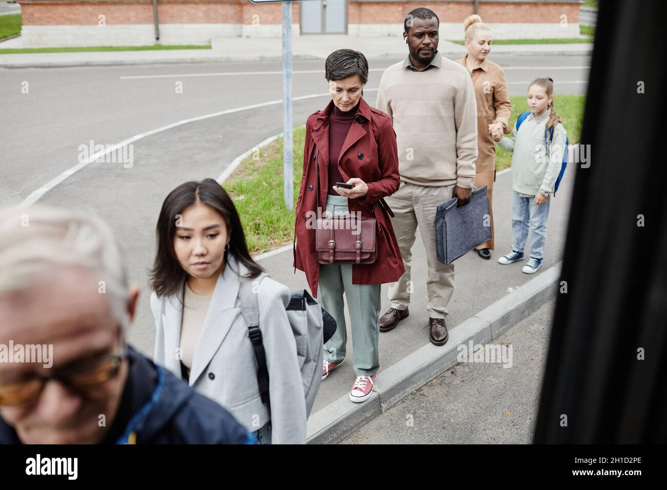Diverse group of people standing in line at bus stop with social ...