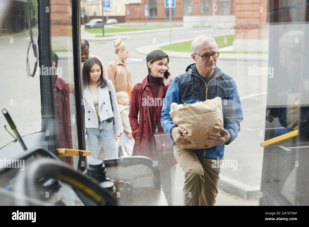 Through glass view at diverse group of people standing in line at bus ...