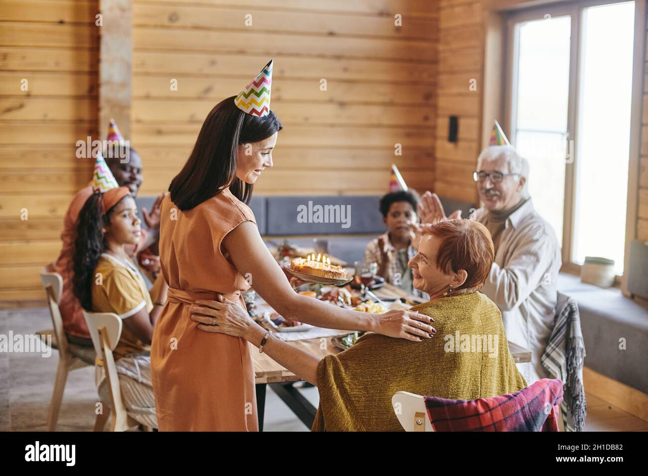 Daughter carrying birthday cake and congratulating her mother with ...
