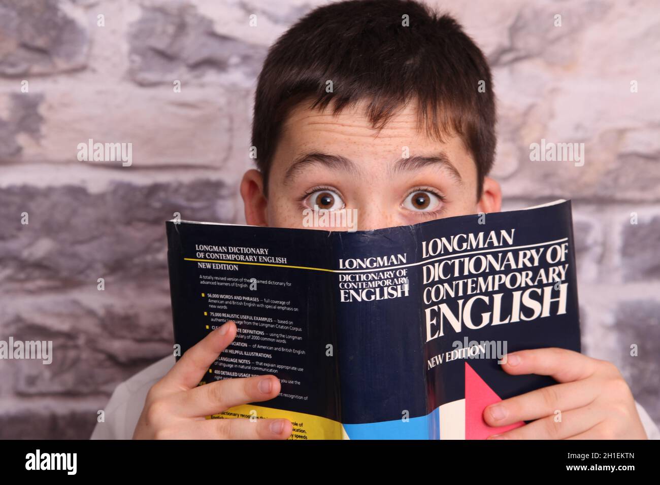 School boy looking peeking over the top of Longmans Dictionary of ...