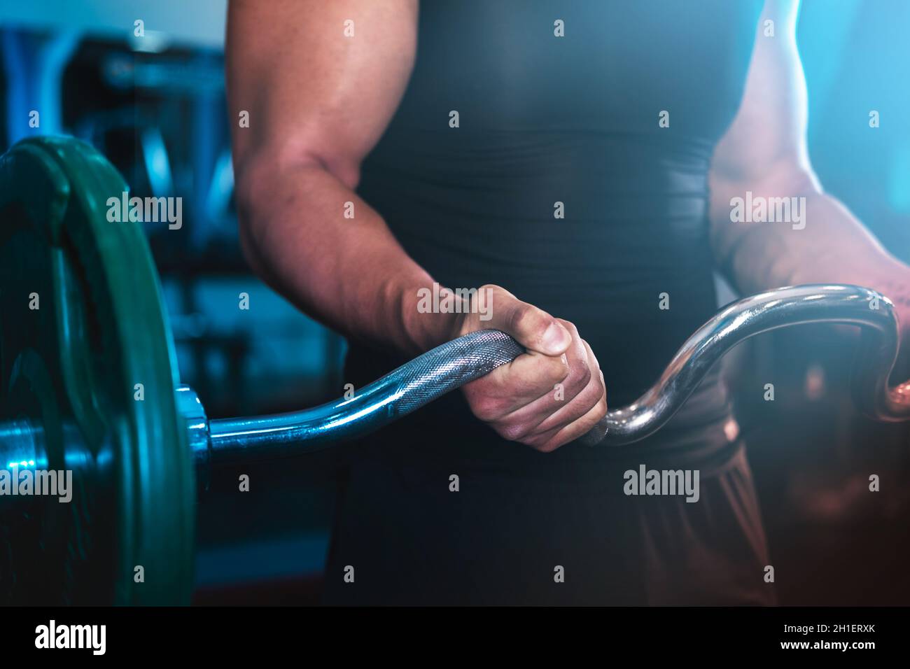 A young athlete does exercises for biceps, a barbell with a curved bar ...