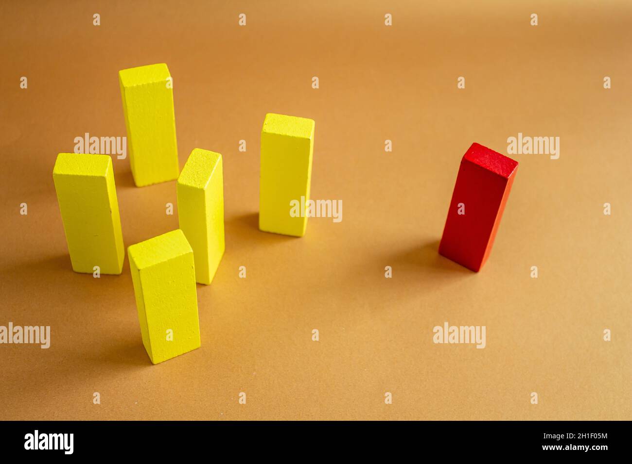 A single red block standing away from a group of yellow wooden blocks ...