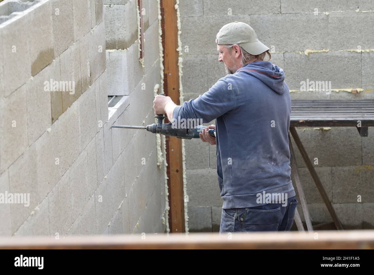 Worker building a wall on a house and drilling into a wall with manual ...