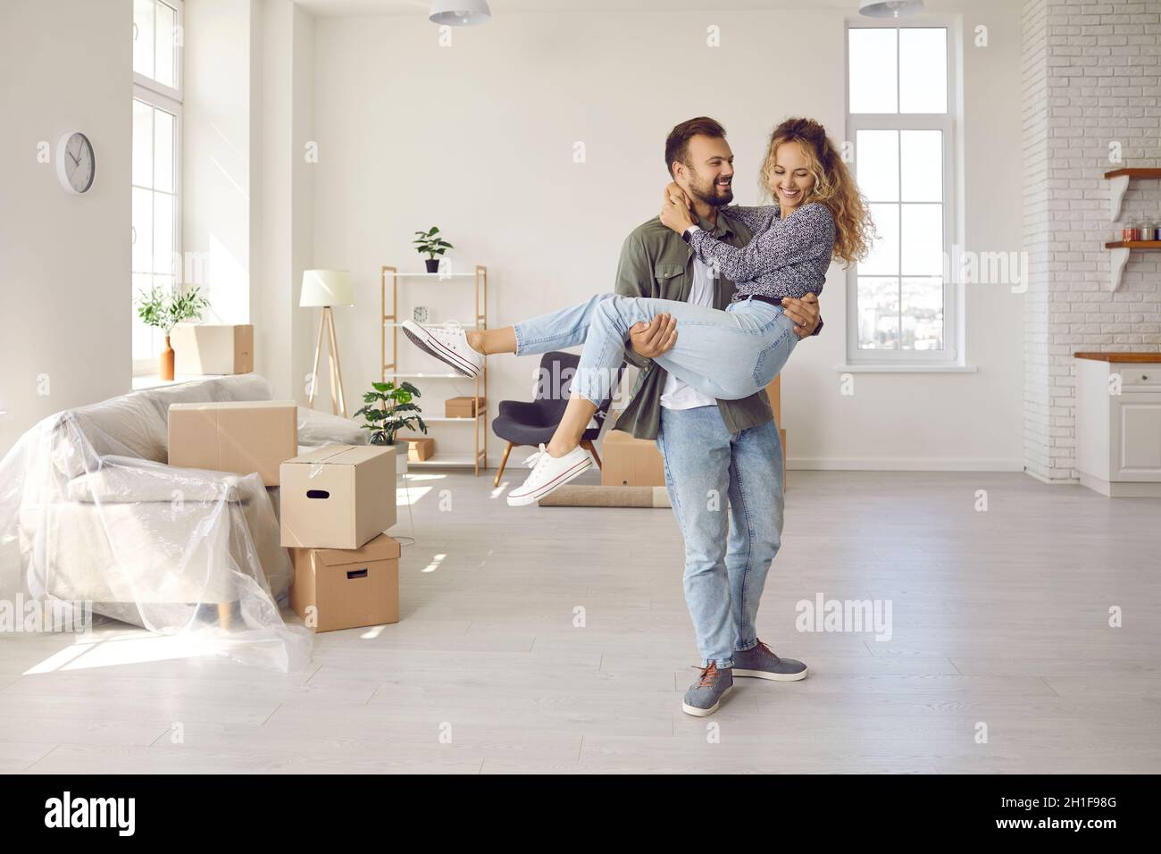 Happy young man carrying his wife in his arms while having fun in their ...