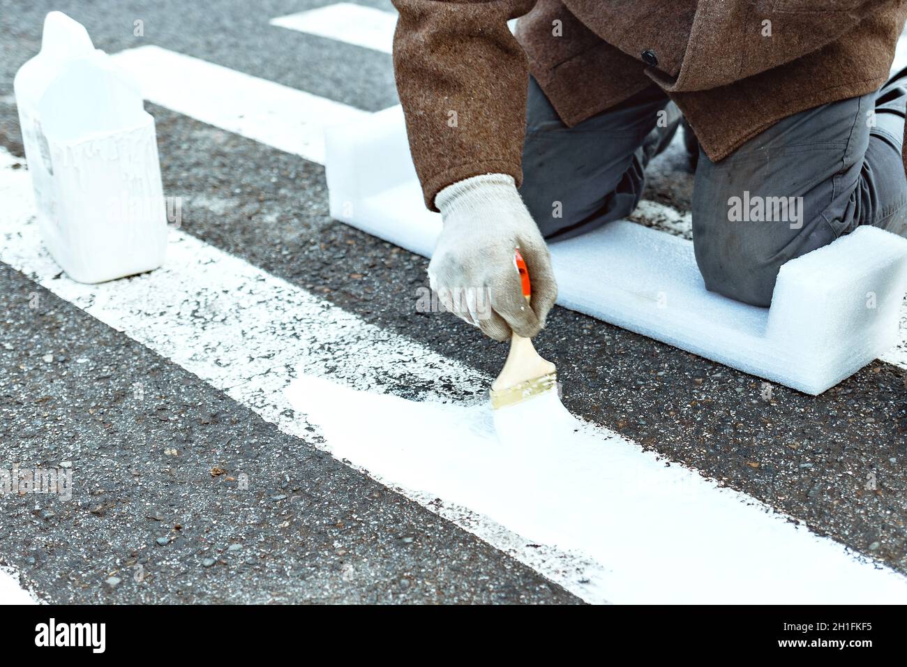 A man paints with a brush on the asphalt markings for a pedestrian ...
