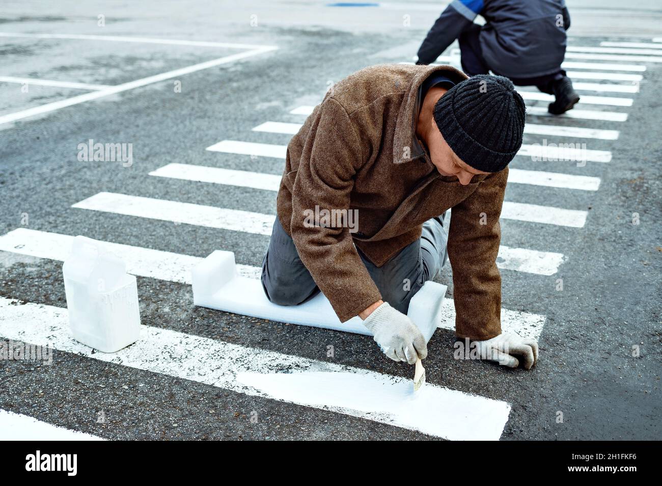 A man paints with a brush on the asphalt markings for a pedestrian ...