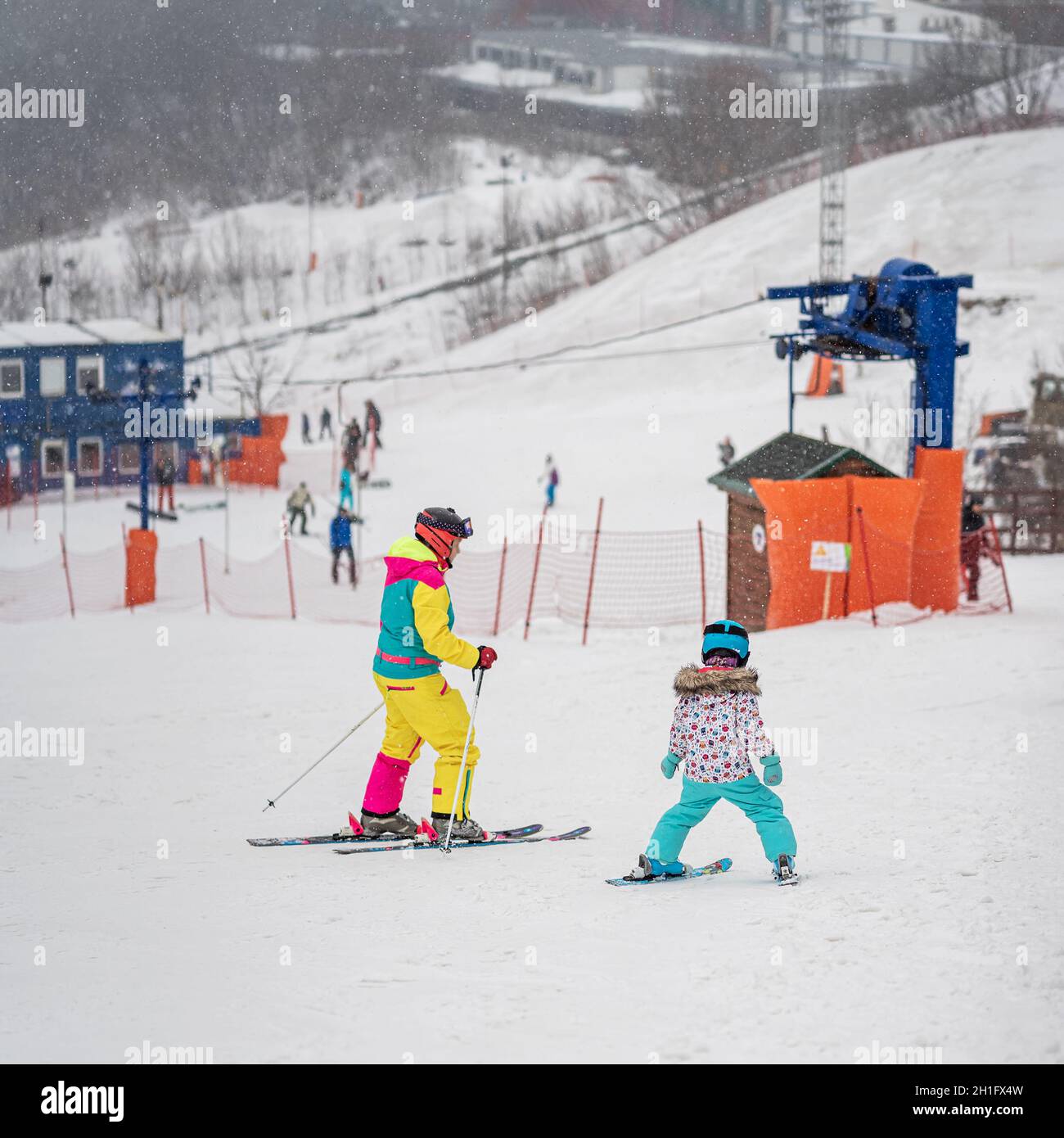 Alpine skiing training, child and coach on ski slope, rear view. Winter ...