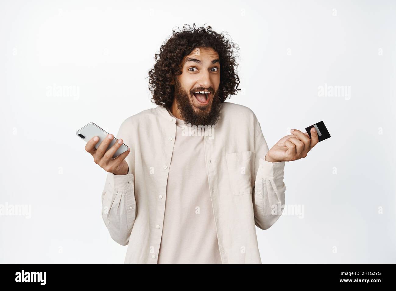 Happy careless young man holding mobile phone and credit card ...