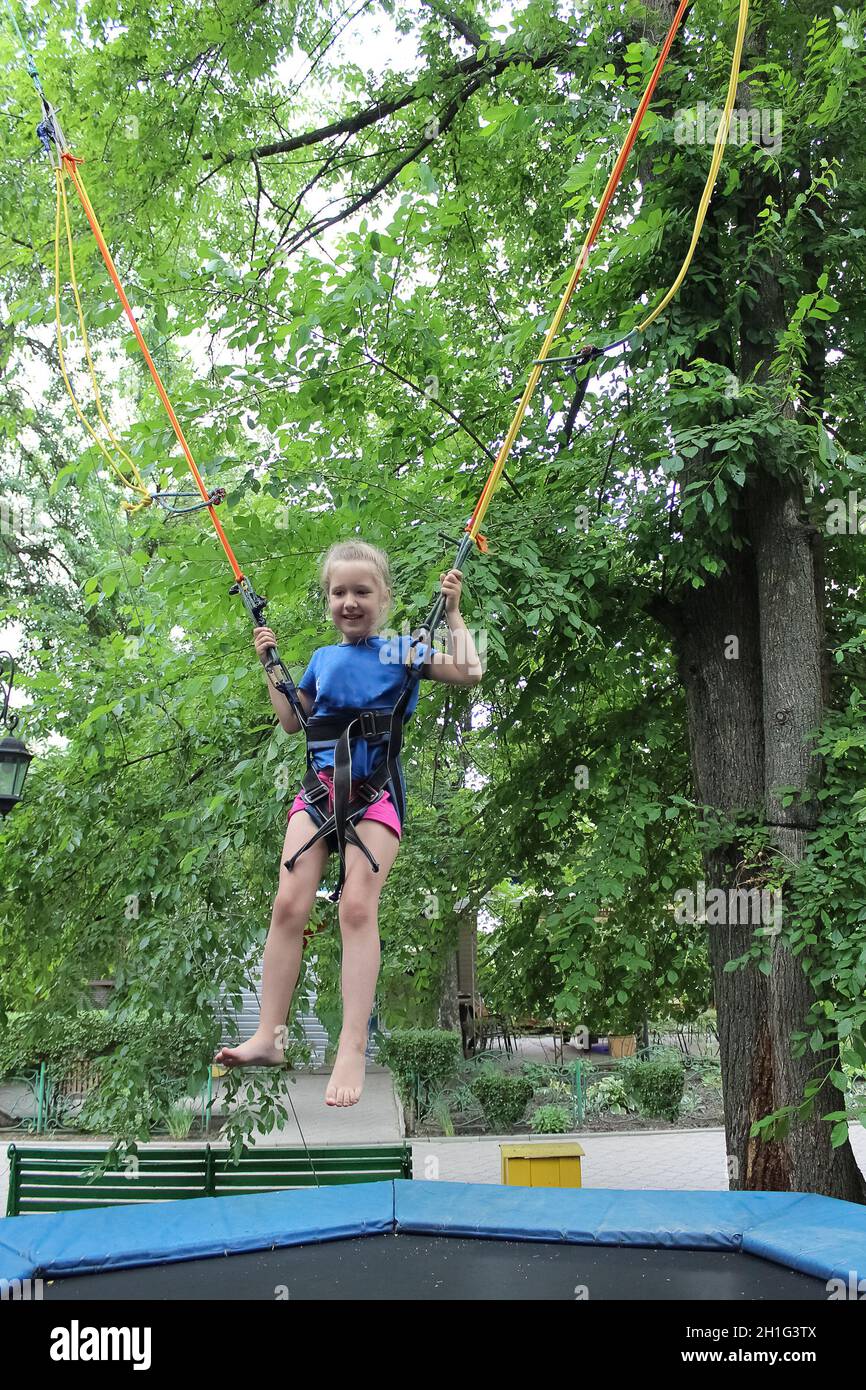 The smiling happy girl jumping with bungee in trampoline at park ...