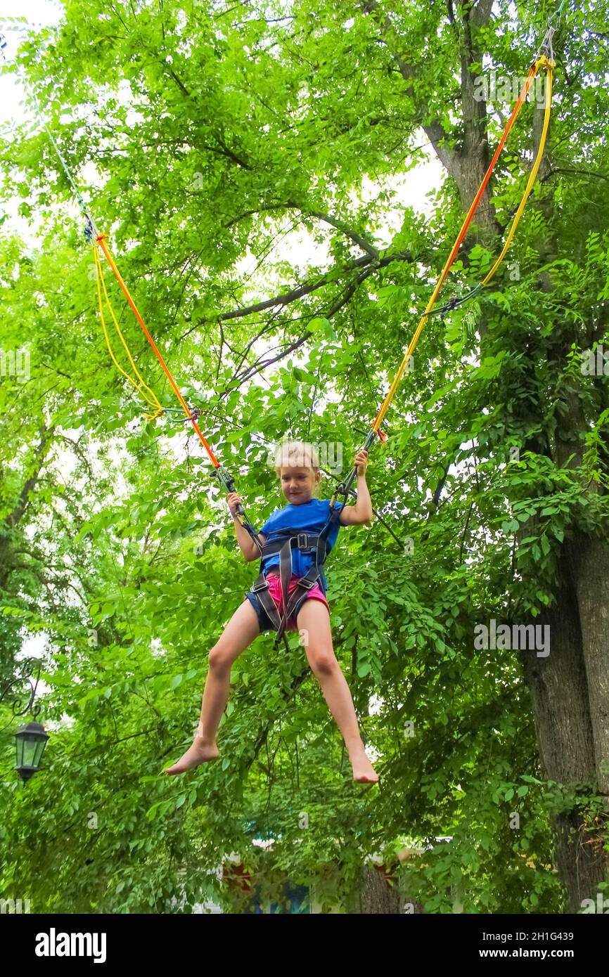 The smiling happy girl jumping with bungee in trampoline at park ...