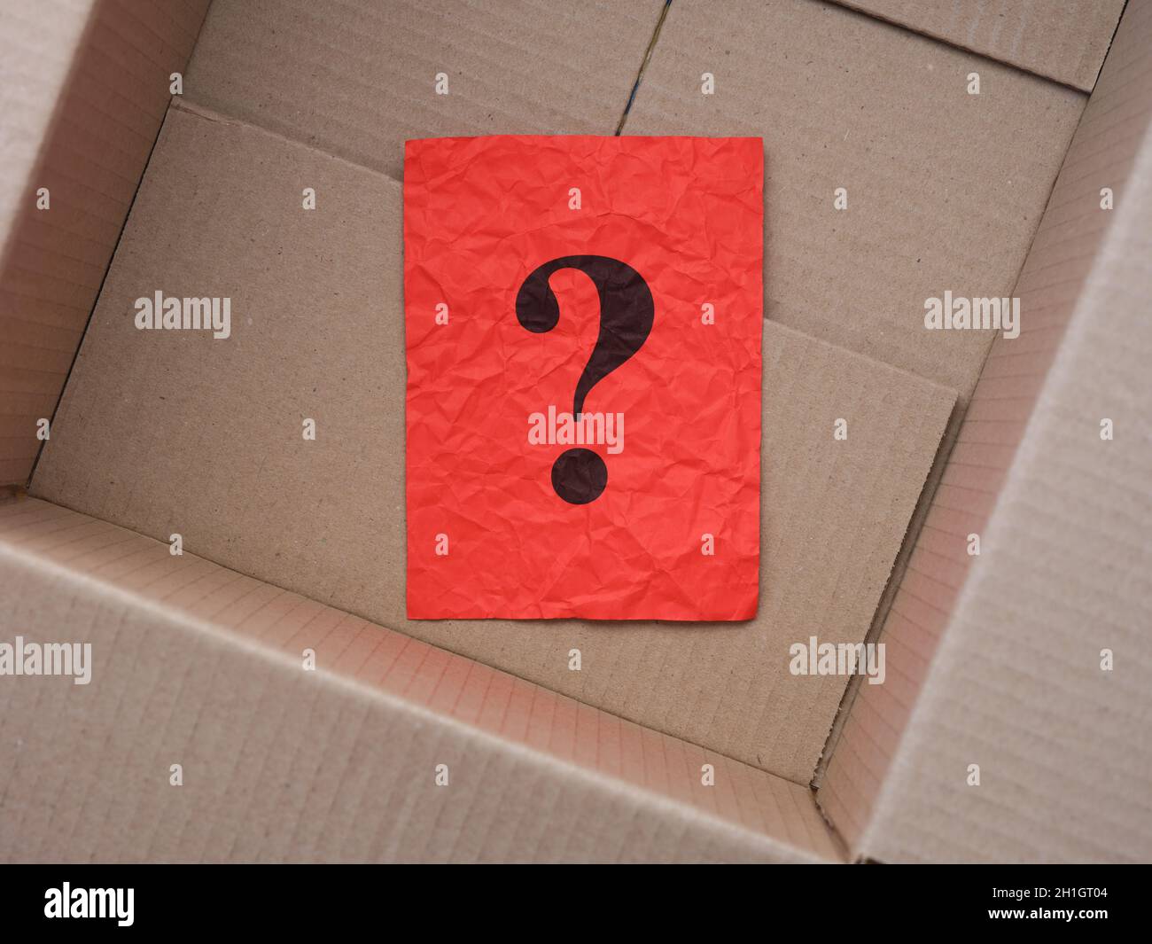 A crumpled red piece of paper with a question mark on it in a cardboard ...