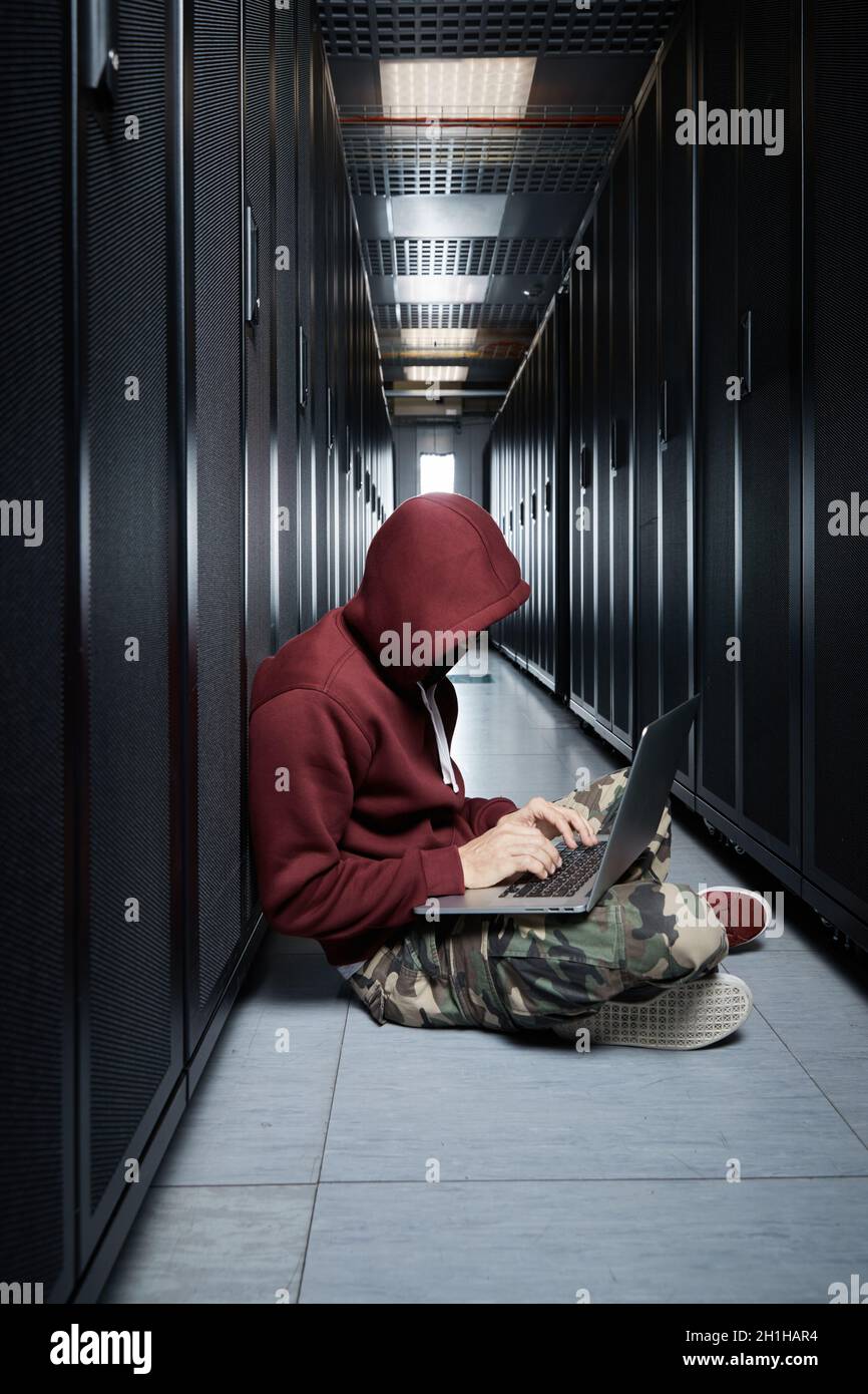 The hacker in a hood sits with the computer among servers, the burglar ...