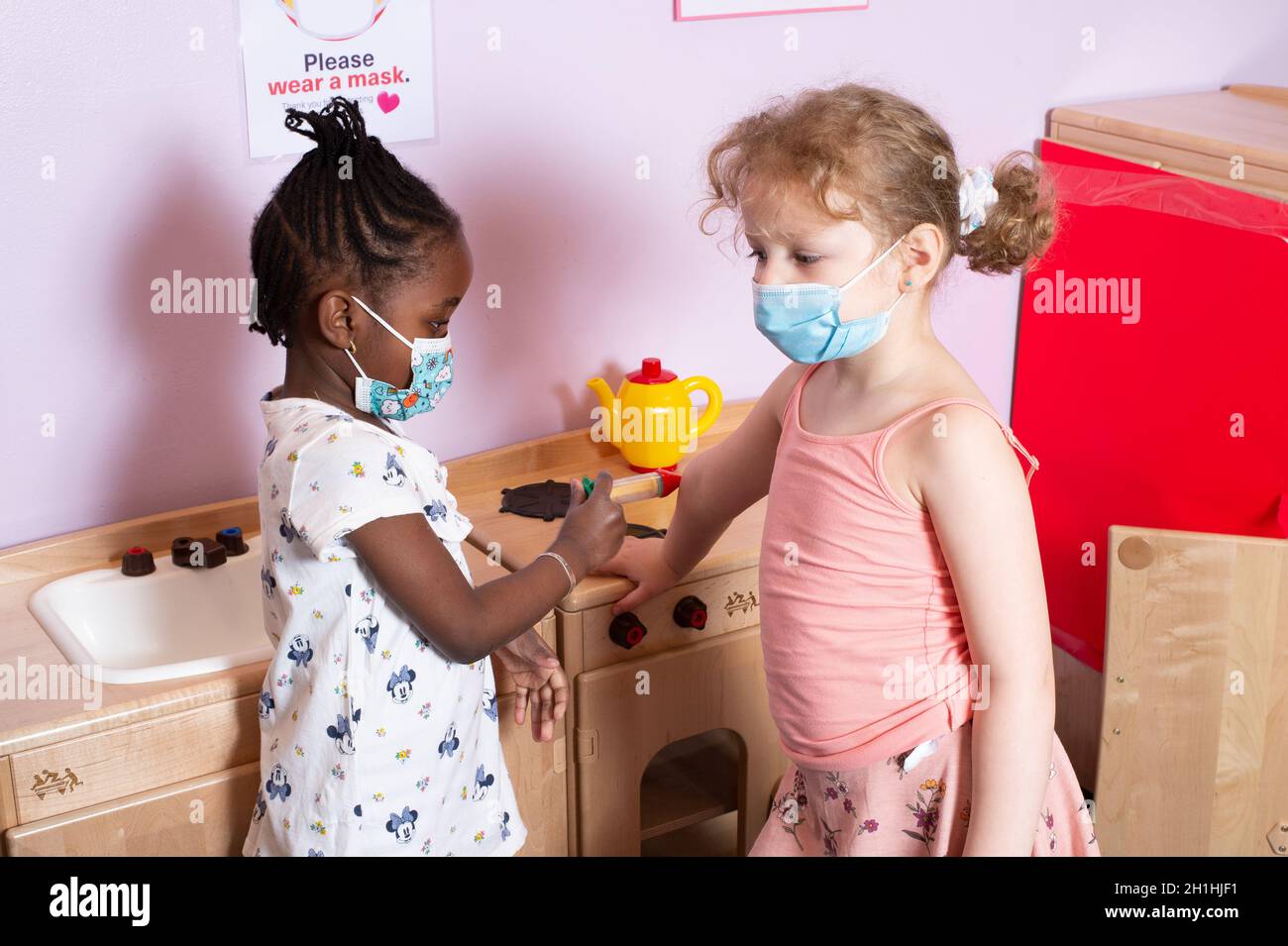 Education preschool 4-5 year olds two girls playing in family area one ...