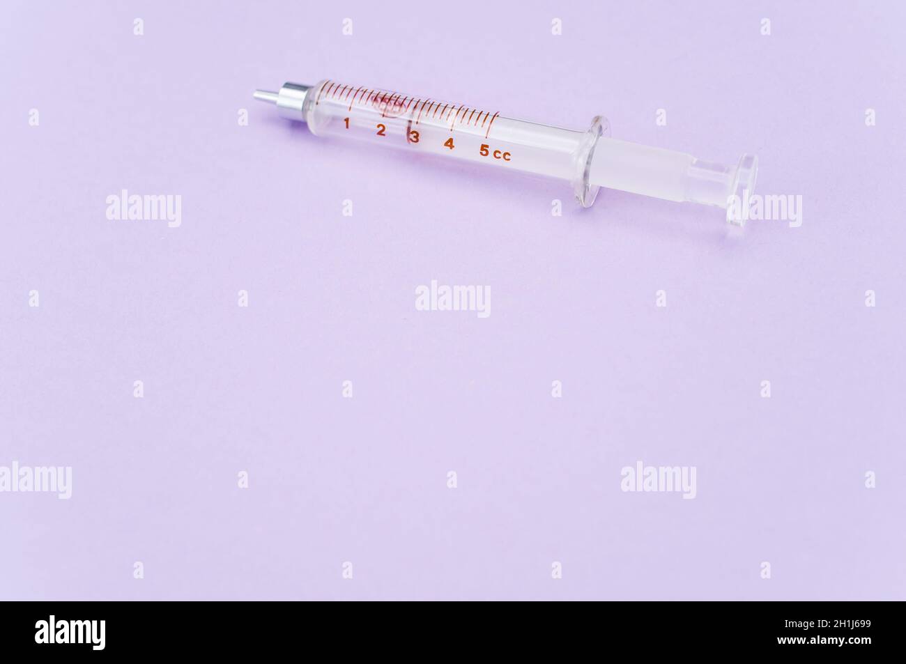 isolated sterilized glass injection syringe on a lilac paper background ...