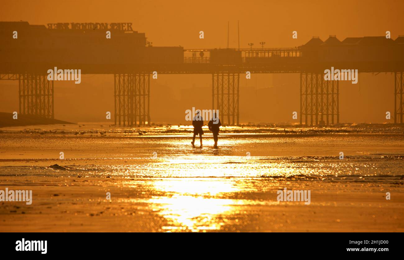 Brighton beach at low tide, sunrise. Silhouetted shapes of two people ...
