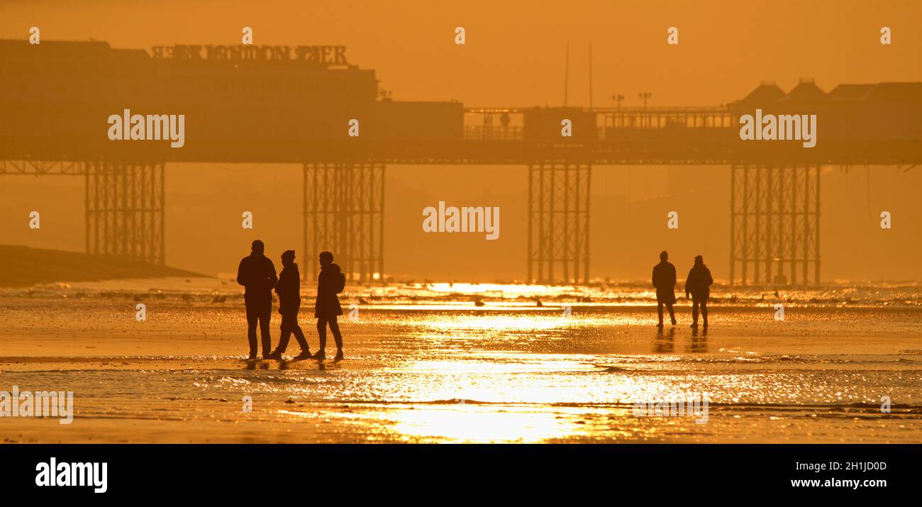 Brighton beach at low tide, sunrise. People walking along sand at low ...