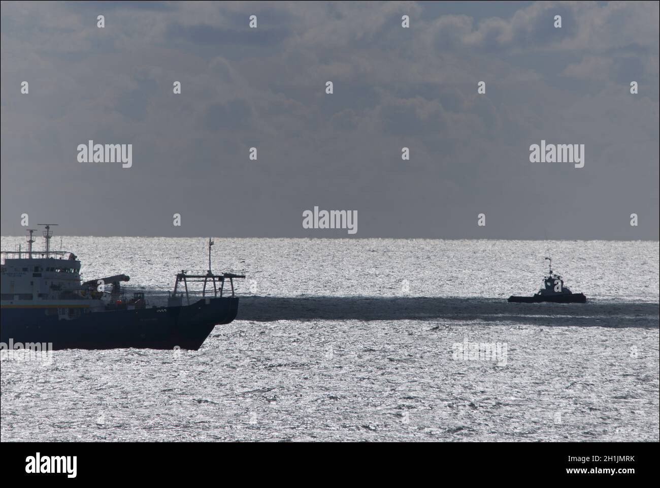 2 boats offshore, photographed as silhouettes in shimmering sunshine ...