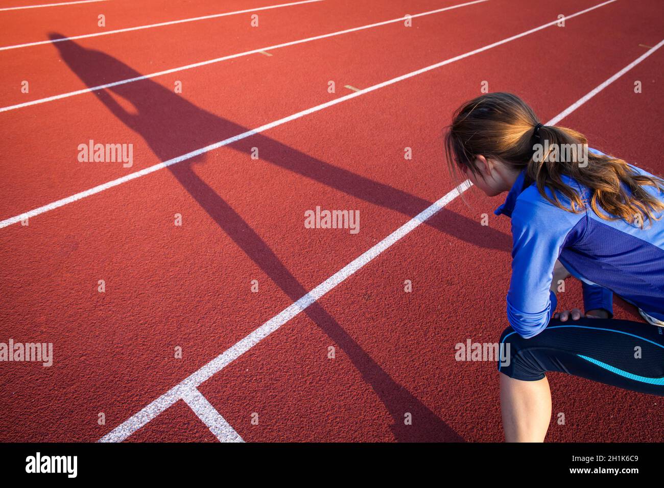 Pretty female runner stretching before her run at a track and field ...