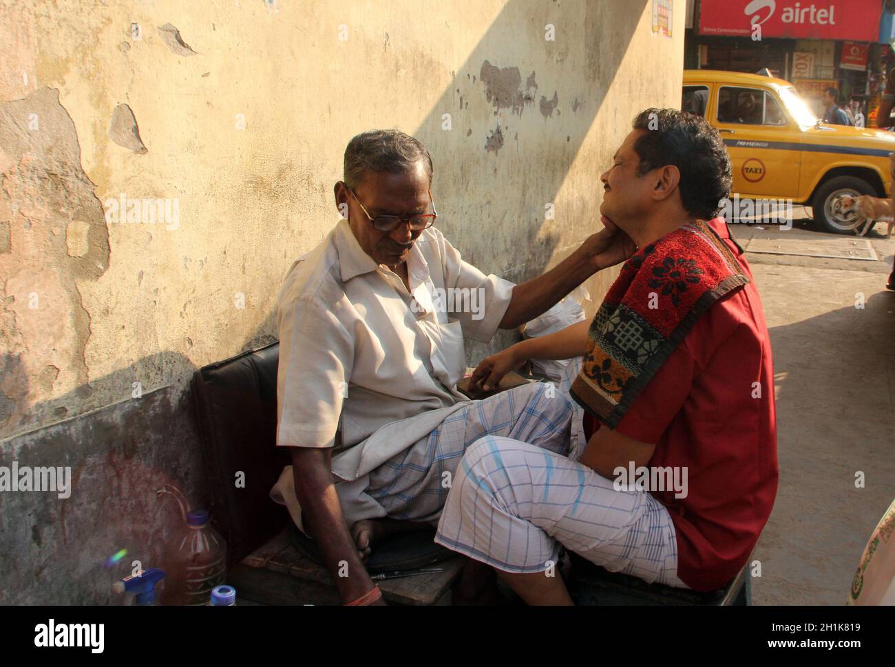 Street barber shaving a man using an open razor blade on a street in ...