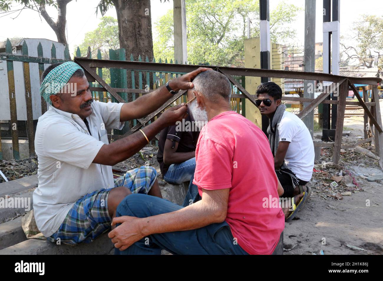 Street barber shaving a man using an open razor blade on a street in ...