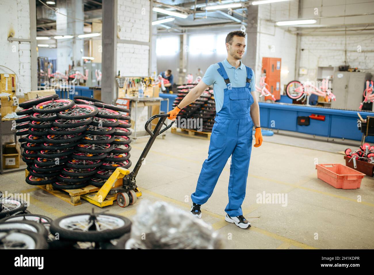 Bicycle factory, worker carries a cart with bike wheels. Male mechanic ...